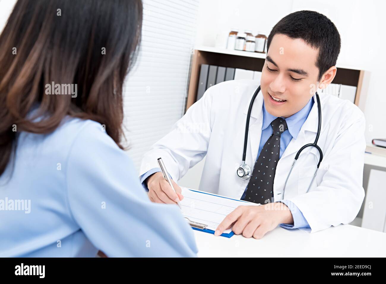 Handsome Asian male doctor noting a female patient medical check up ...
