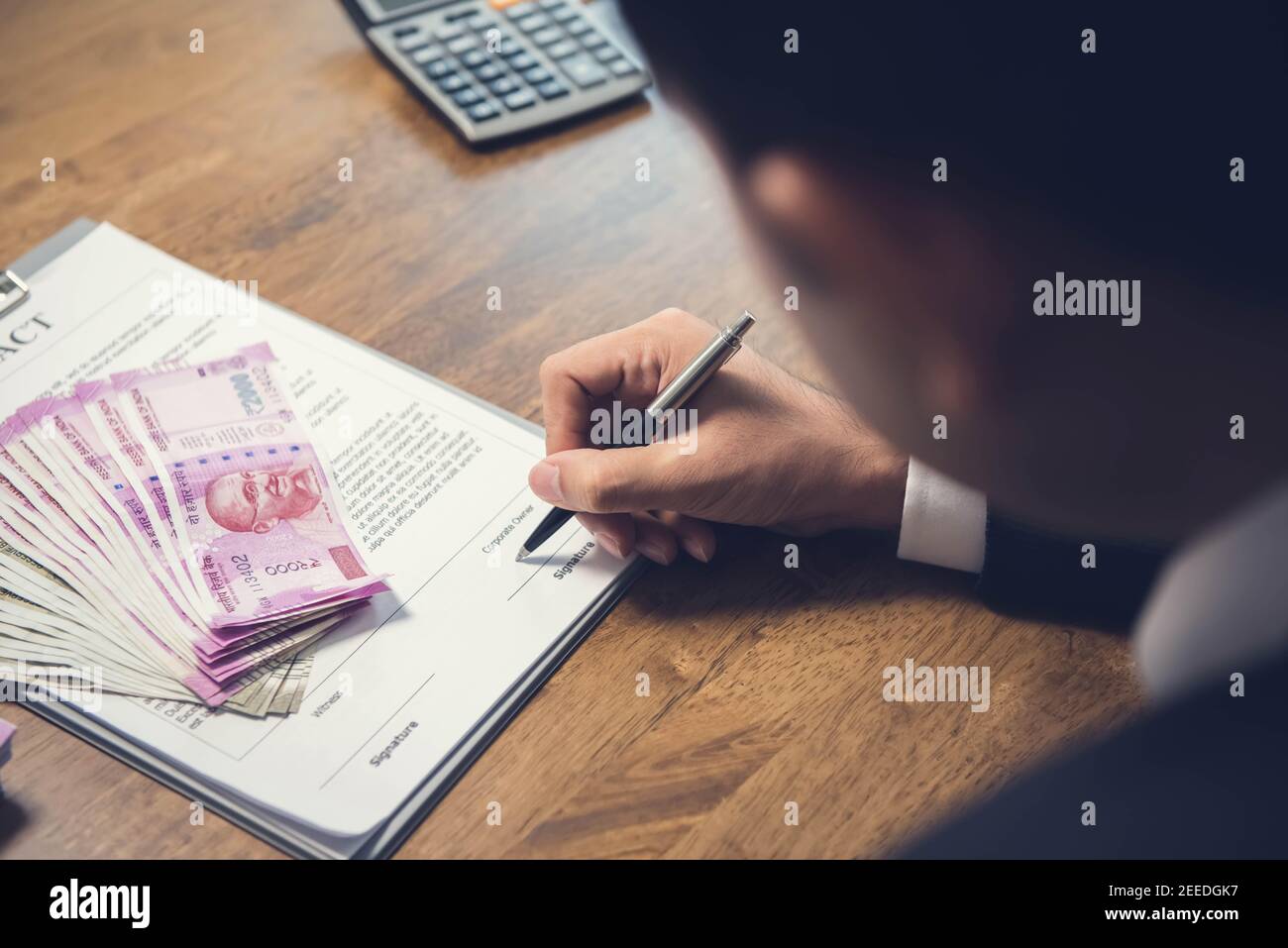 A man signing an agreement with Indian Rupees money on top of document ...