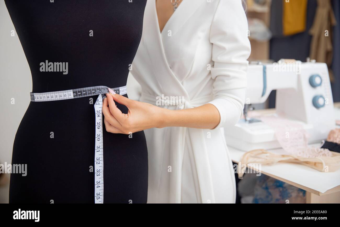 Young woman seamstress tailor takes measurements with measuring tape ...