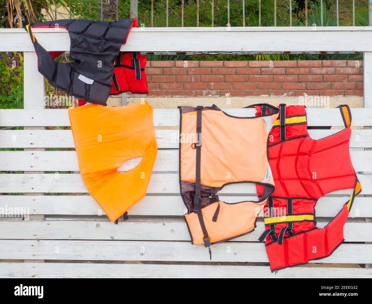 Red and orange life jackets hang on white wooden fence outdoors ...