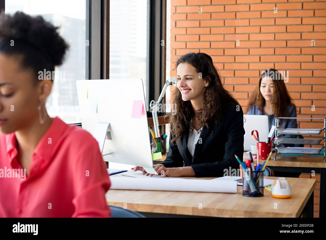 Happy business woman using computer at her working desk in creative ...