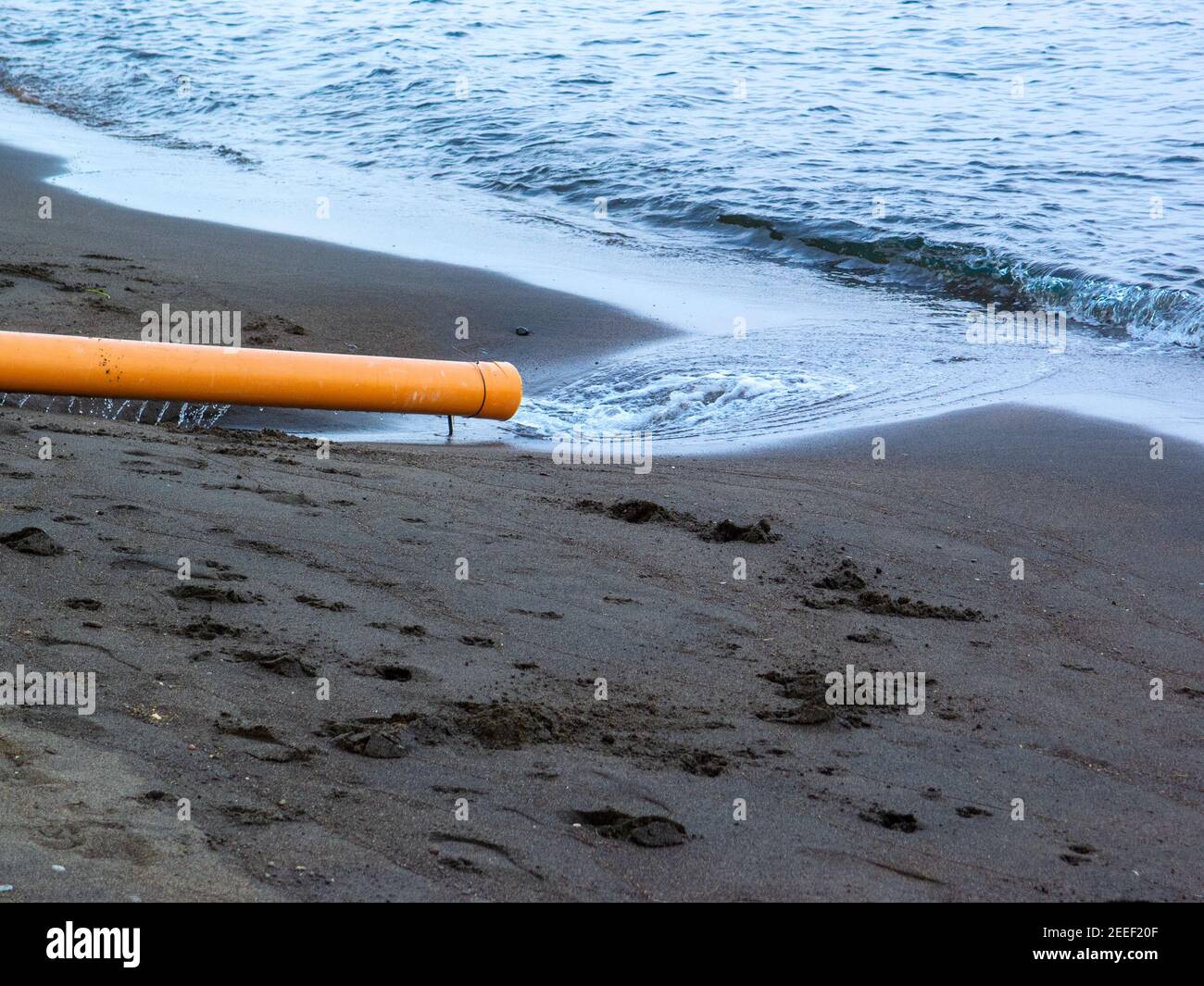 Orange pipe with water poured into sea, beach pollution. Tourist ...