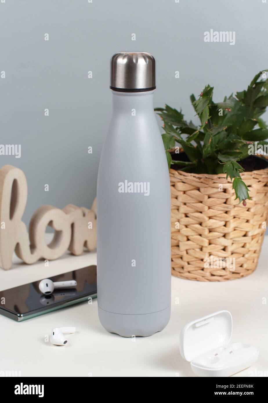 Grey insulated bottle on white desk surrounded by modern gadgets and ...