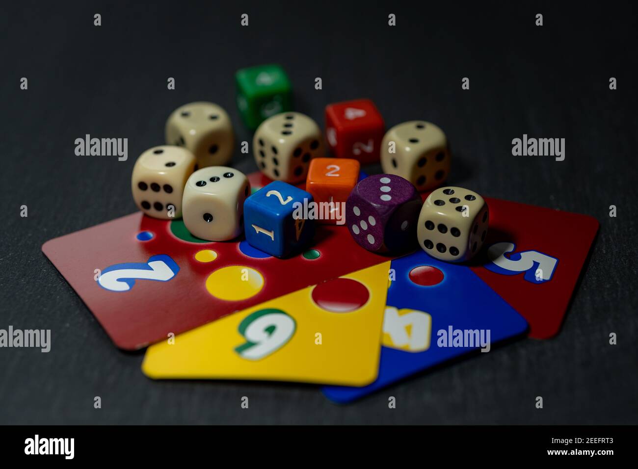 Colourful dice lie on colourful playing cards against a dark, neutral ...