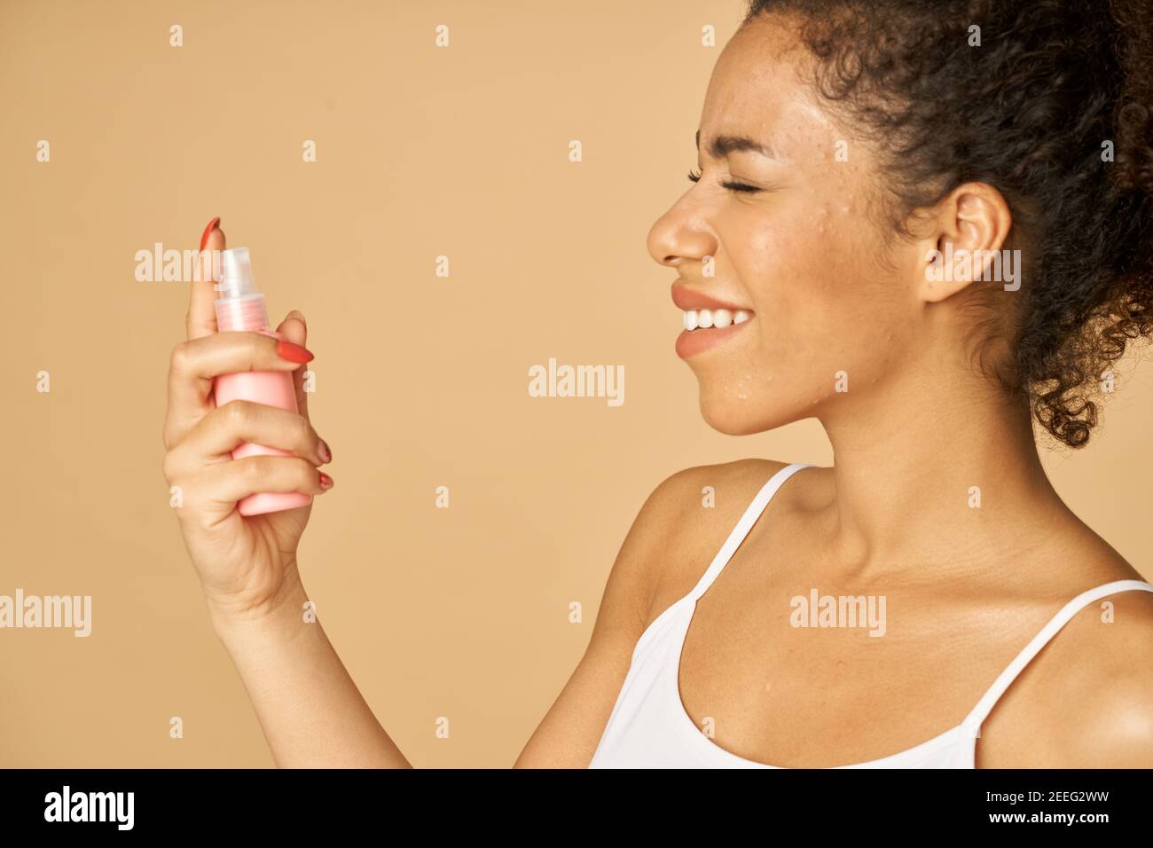 Portrait of attractive young woman applying spray water on face, posing ...