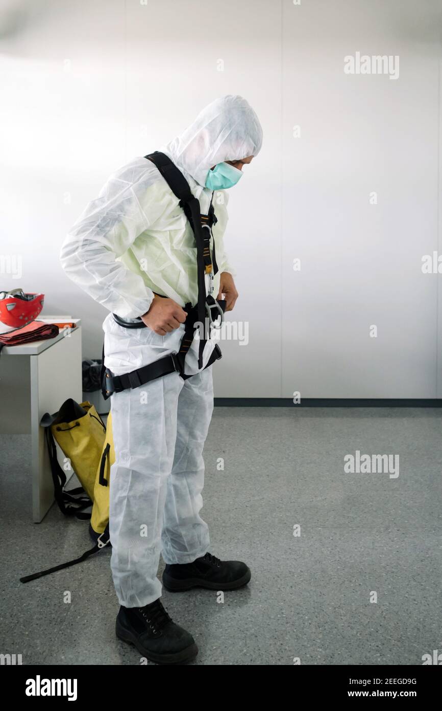 Concept: work. Man in nbc suit putting on a harness and climbing ...