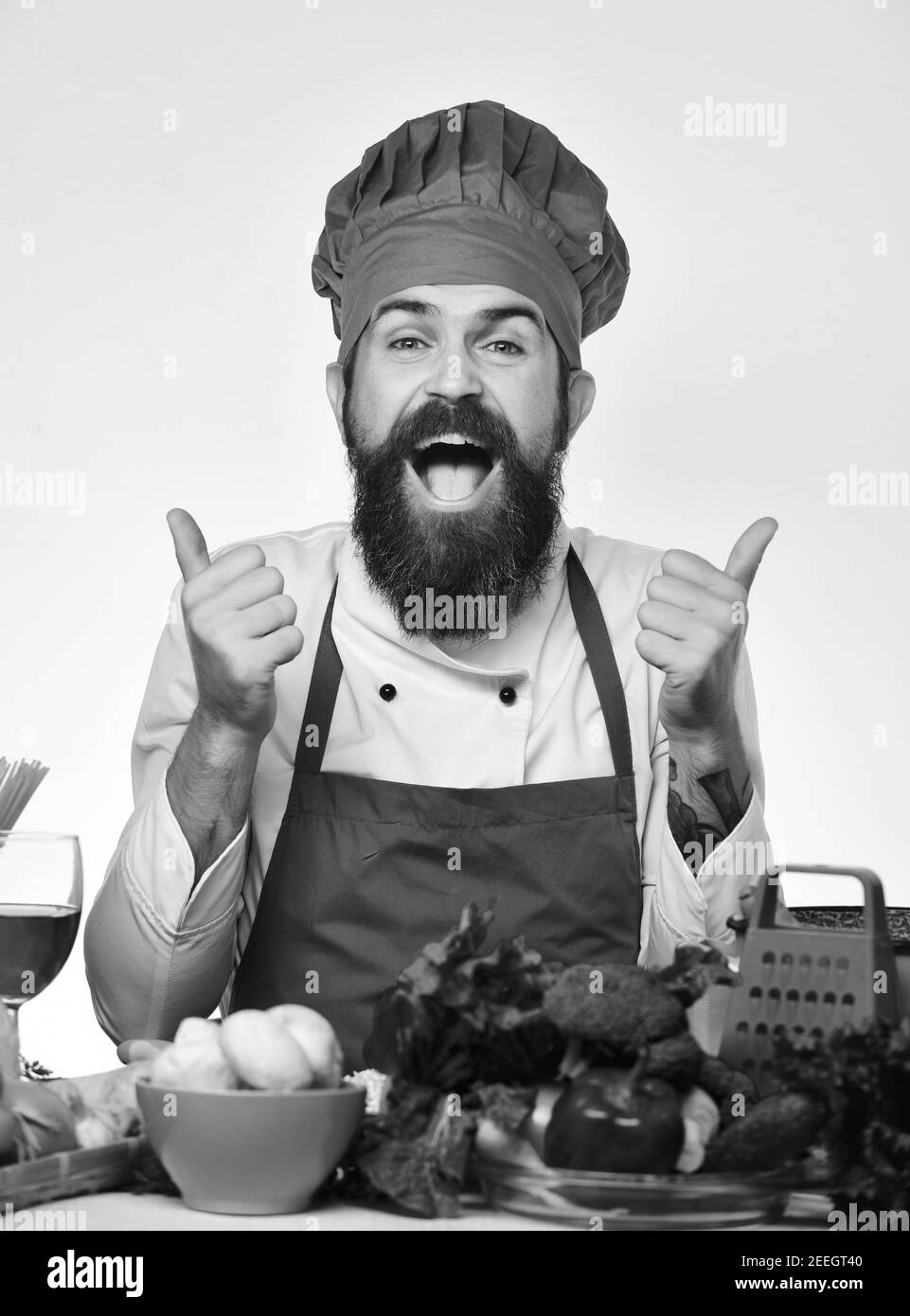 Cook with cheerful face in burgundy uniform sits by kitchen table with ...