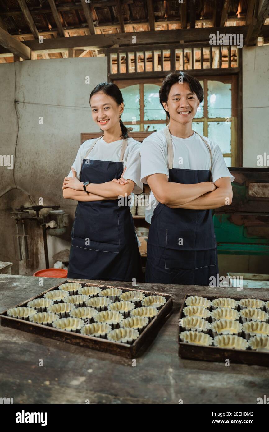 Young couple wearing aprons with their arms crossed confidently as they ...