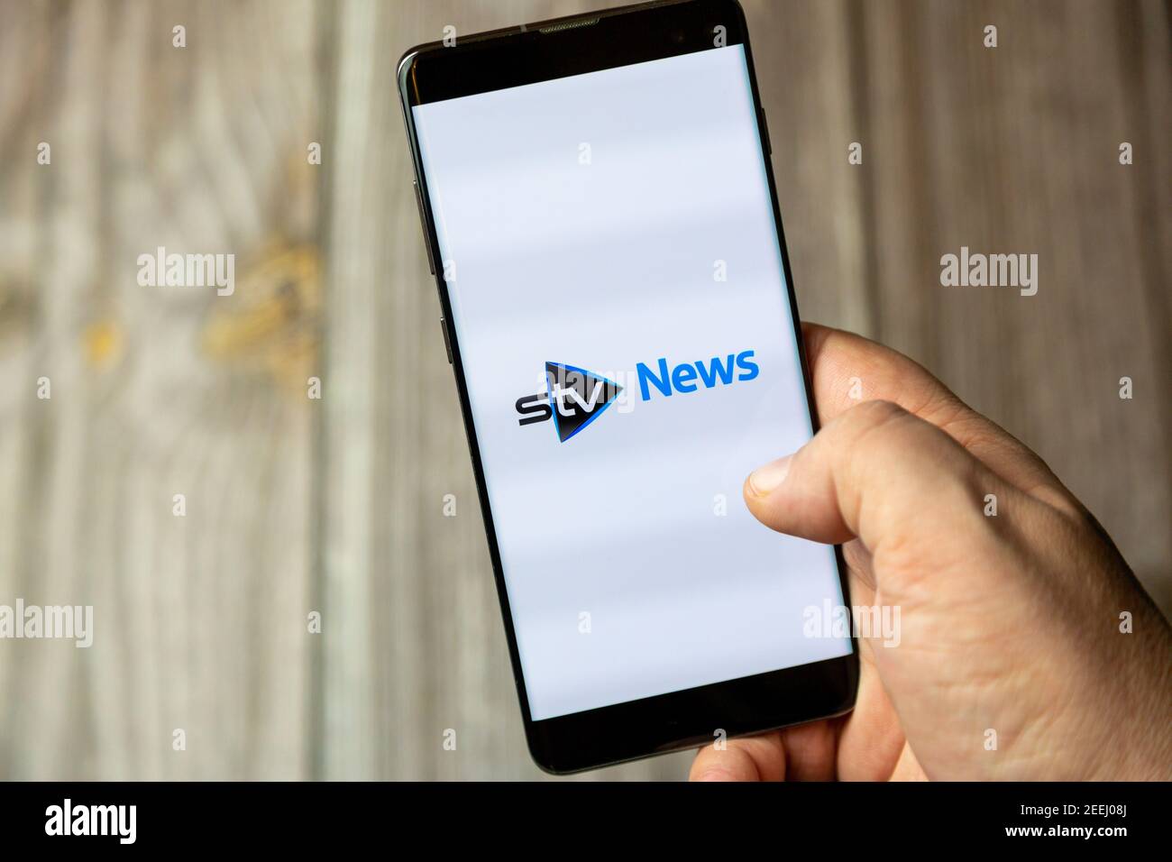 A mobile phone or cell phone being held in a hand with the STV news app ...