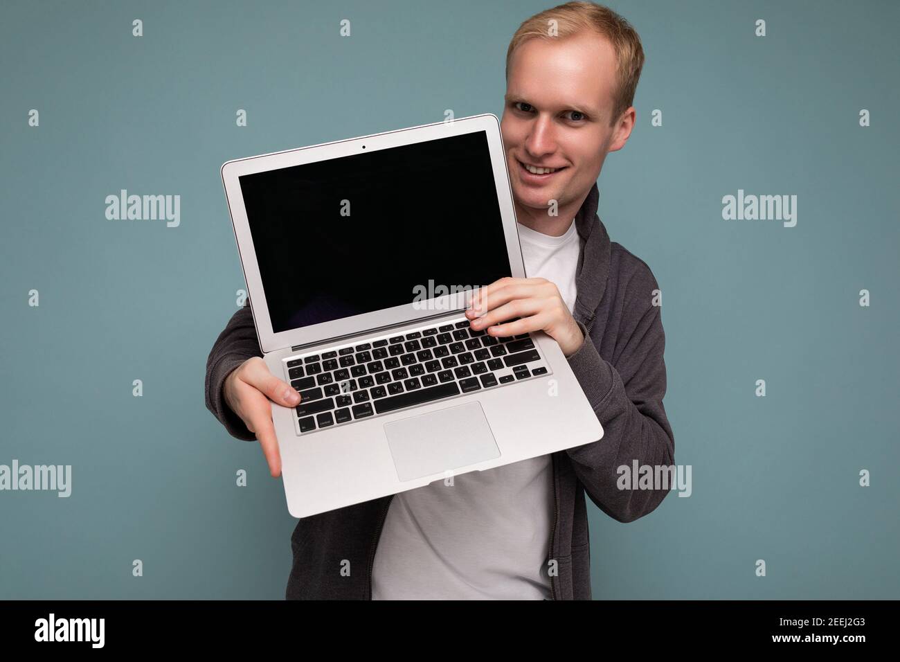 Close-up portrait of handsome smiling blonde man holding computer ...