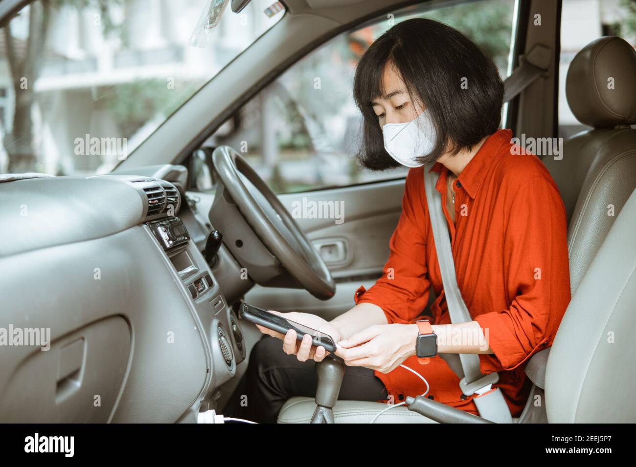 asian Woman in protective mask driving a car on road. charge her phone ...