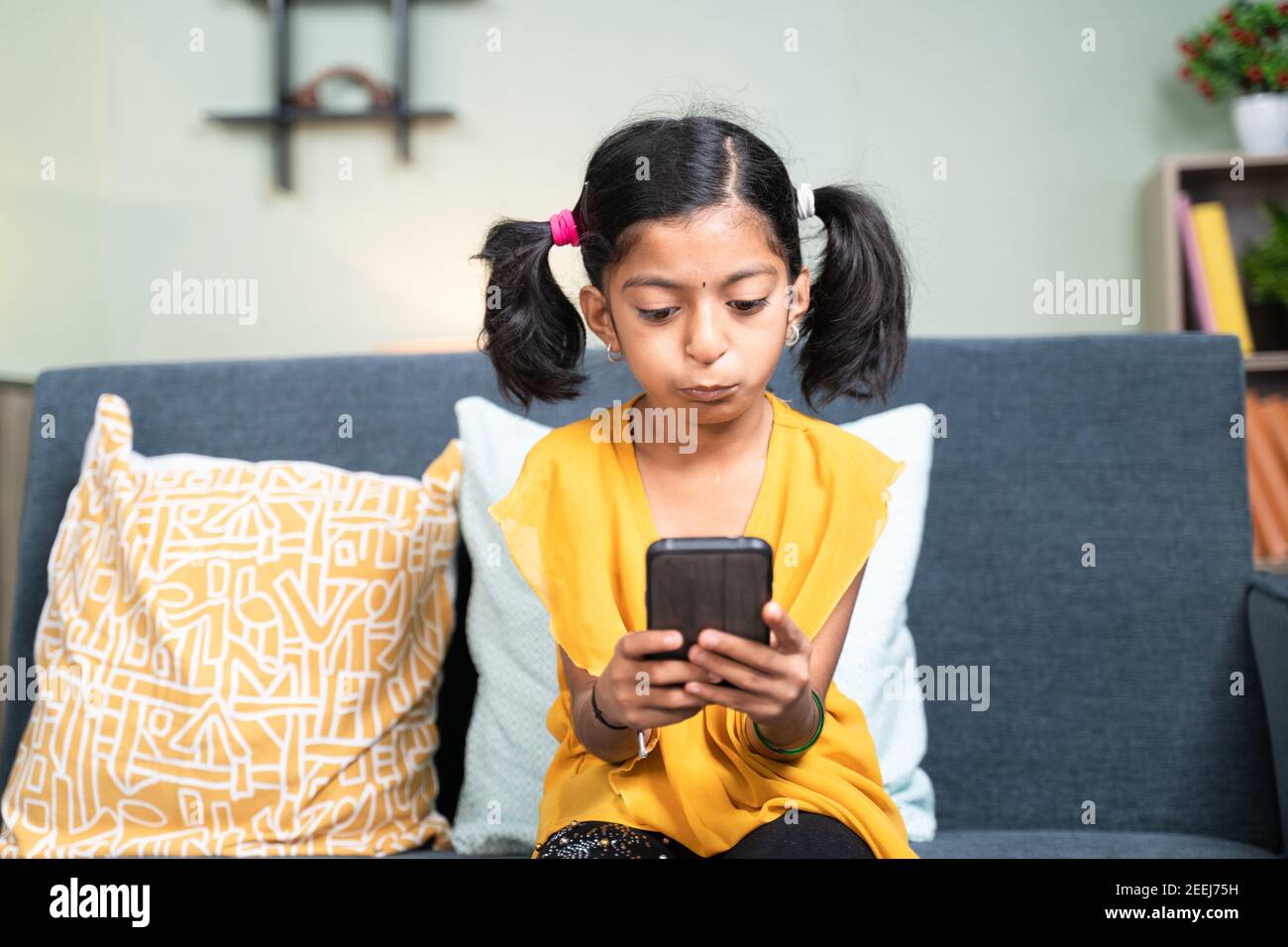 Young girl kid using mobile phone while sitting on sofa in bending head ...