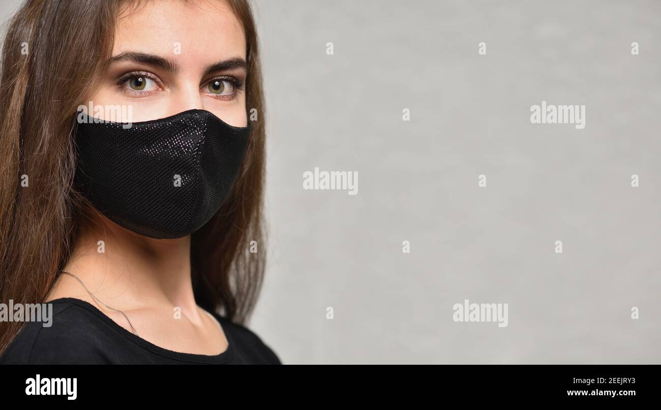 Close up face of young woman in protective black face mask on gray ...