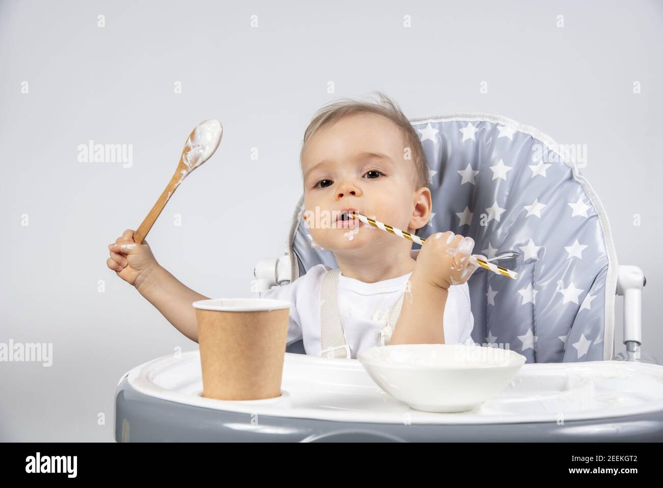 Little beautiful child eating a wooden spoon of yogurt from a plate and ...