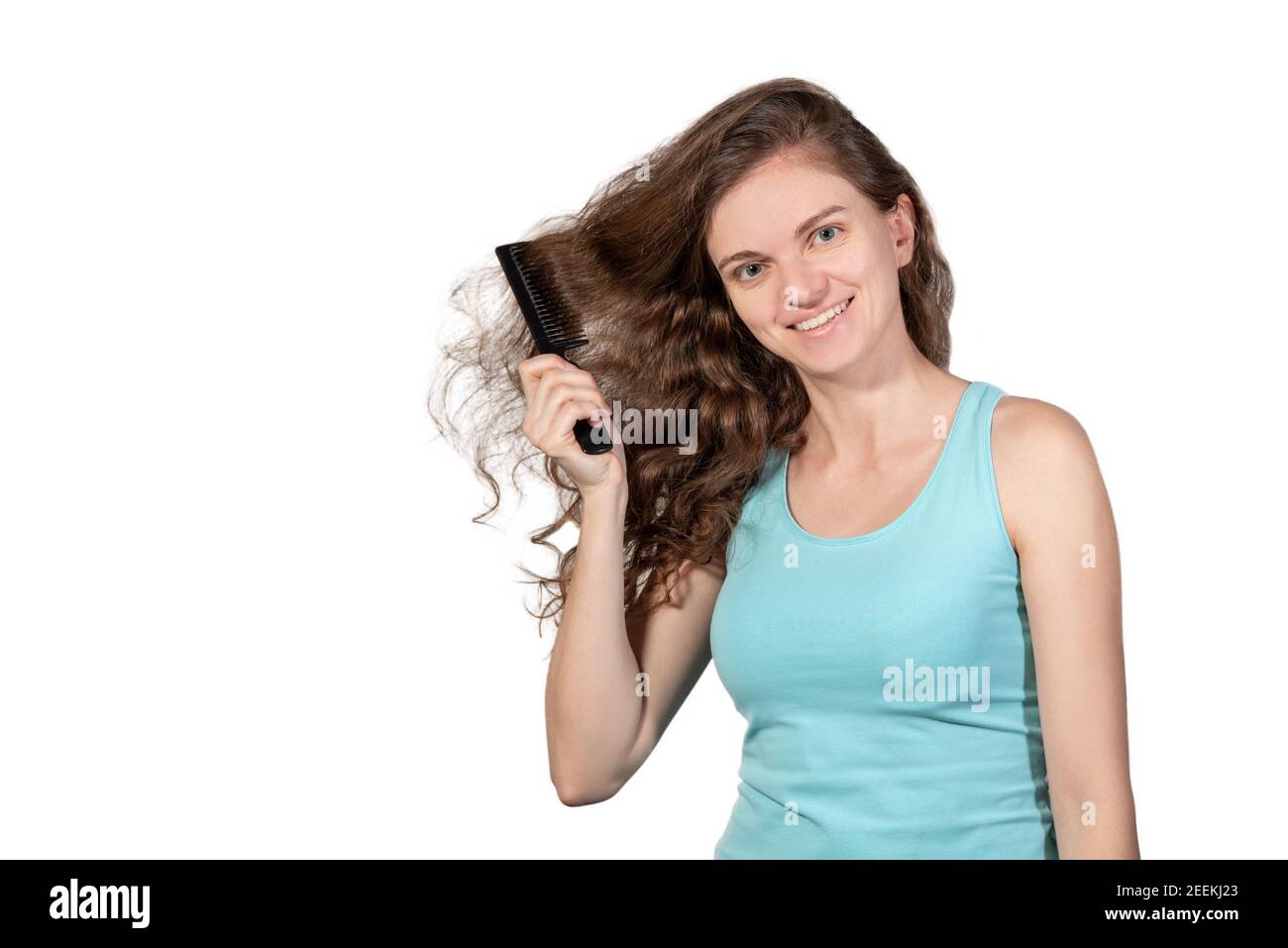 Beautiful brunette girl combing curly long hair with a comb and smiling ...