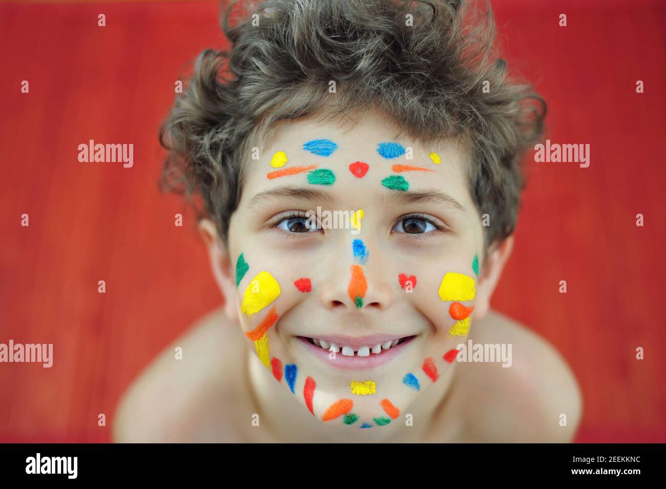 A cute little boy painted colorful stripes on his face with paints ...