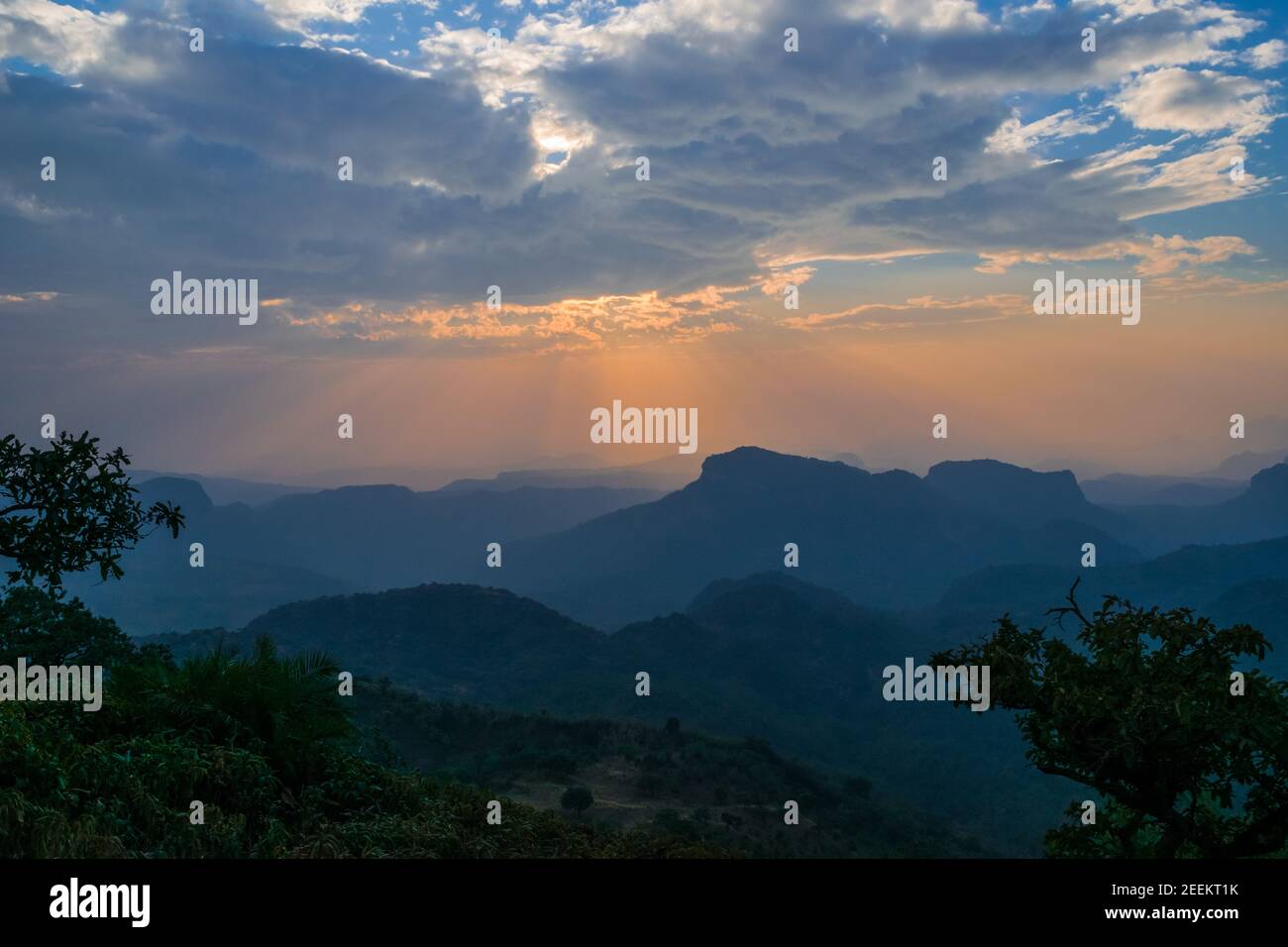 Sun-rays piercing through dark clouds at dusk, engulfs the valley below ...