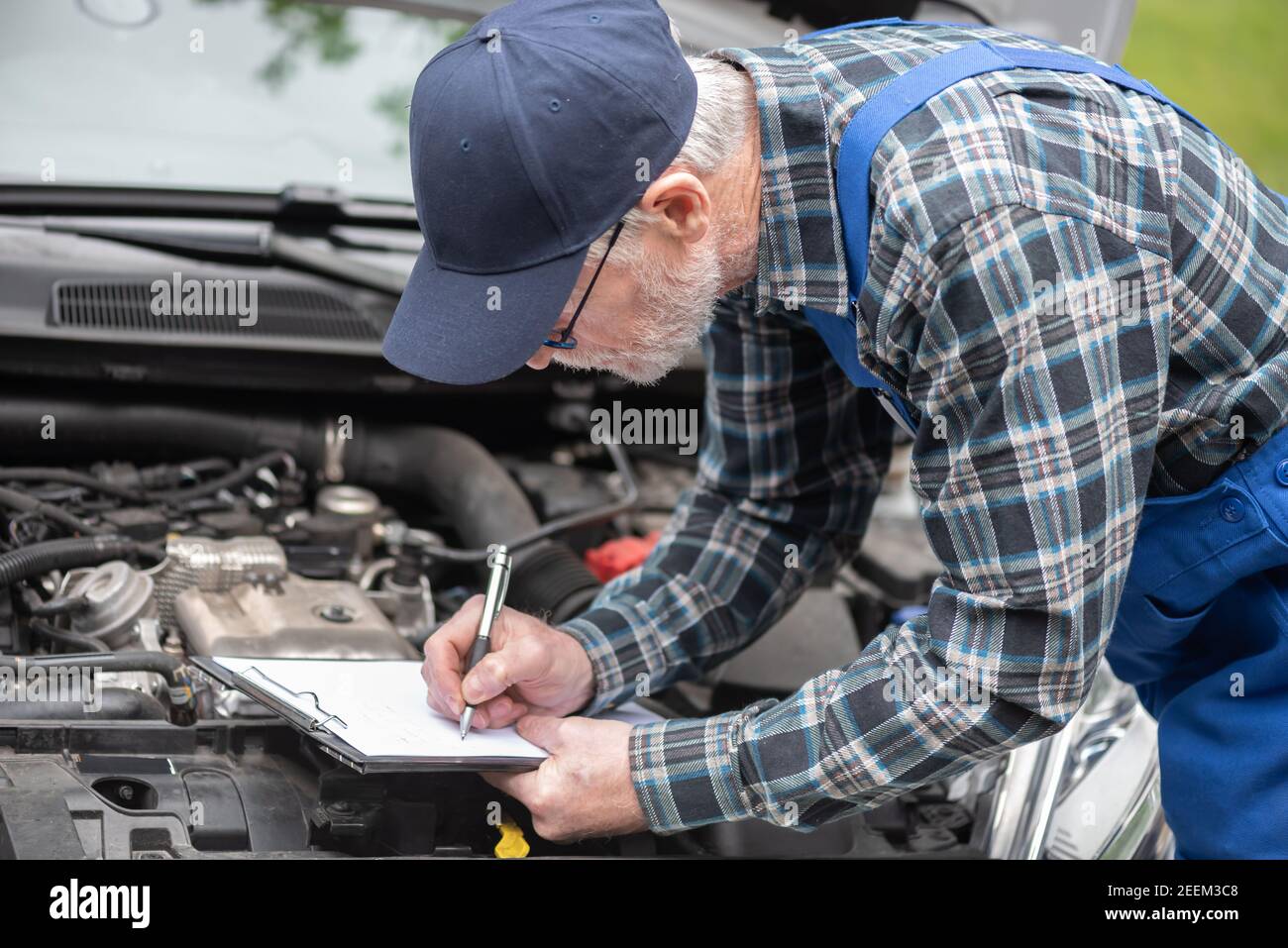 Car mechanic checking a car engine and writing on clipboard Stock Photo ...