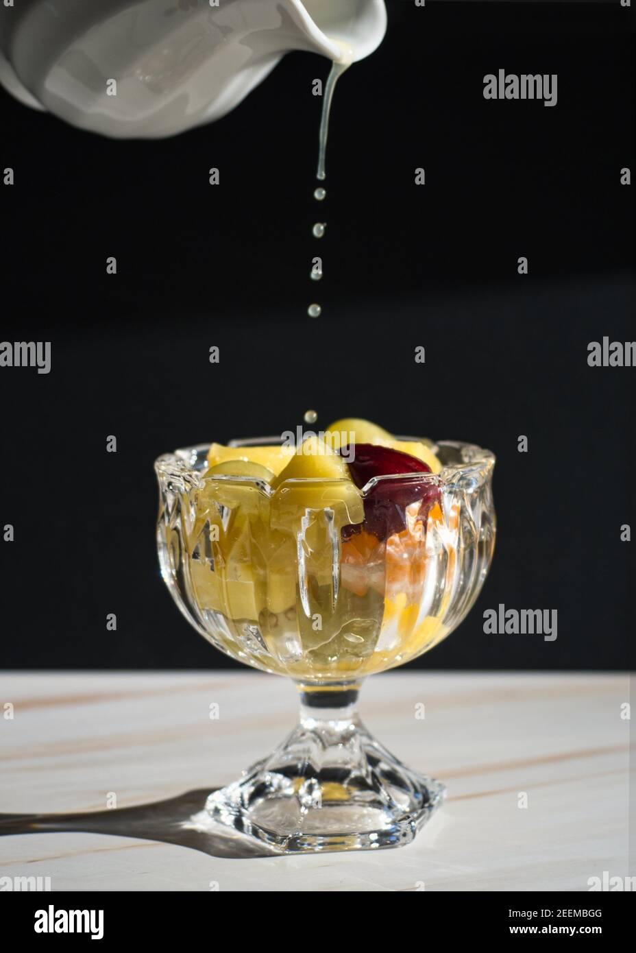 white pitcher pouring juice over pieces of fruit in glass cup with warm ...