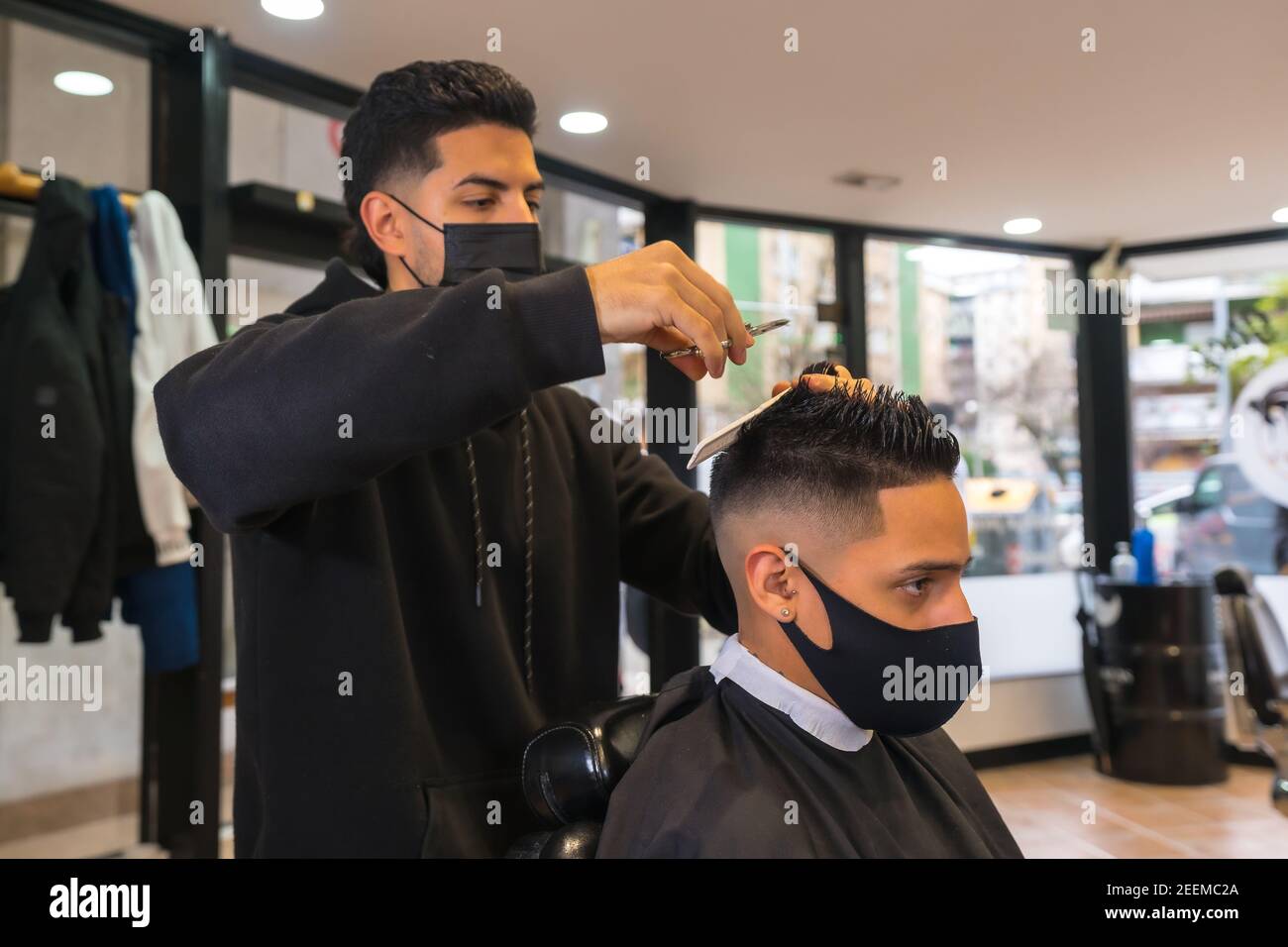 Male hairdresser with a mask cutting the hair of a young man Stock ...