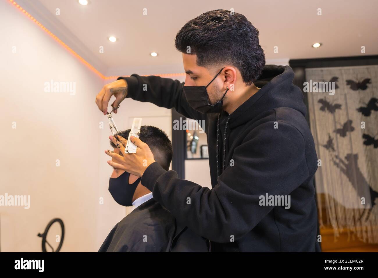 Male hairdresser with a mask cutting the hair of a young man Stock ...