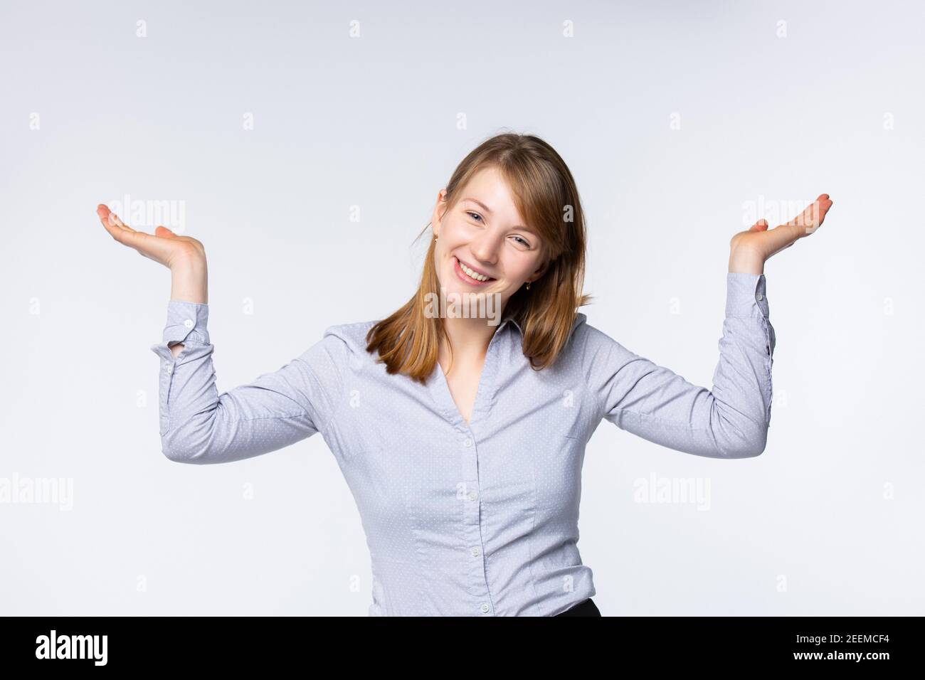Studio portrait of a happy young blonde, raising her hands in a gesture ...