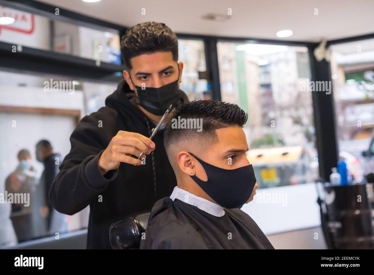 Male hairdresser with a mask finishing the hairstyle of a young male ...