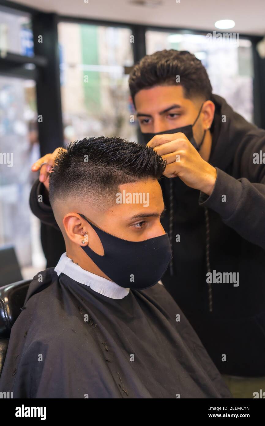 Male hairdresser with a mask cutting the hair of a young man Stock ...