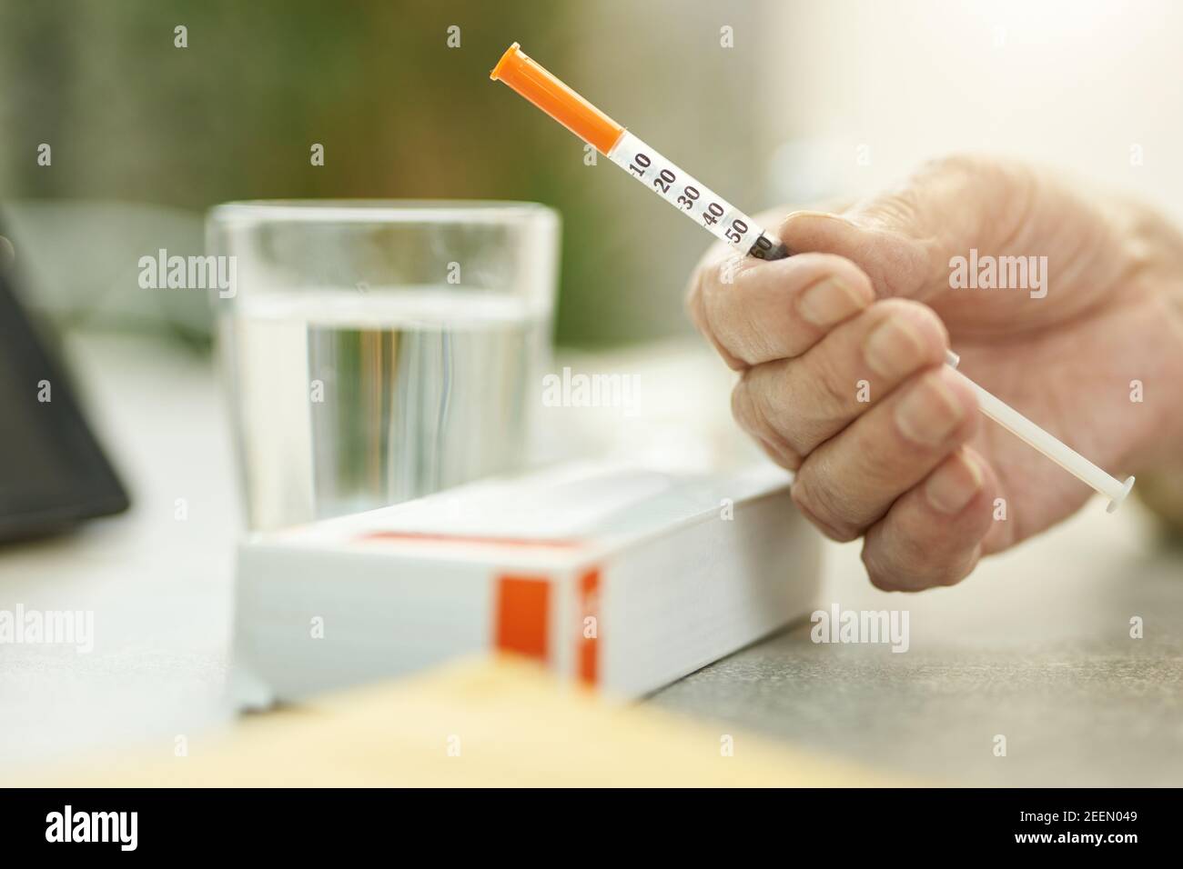 Cropped photo of hand with a thin medical syringe near a glass of water ...