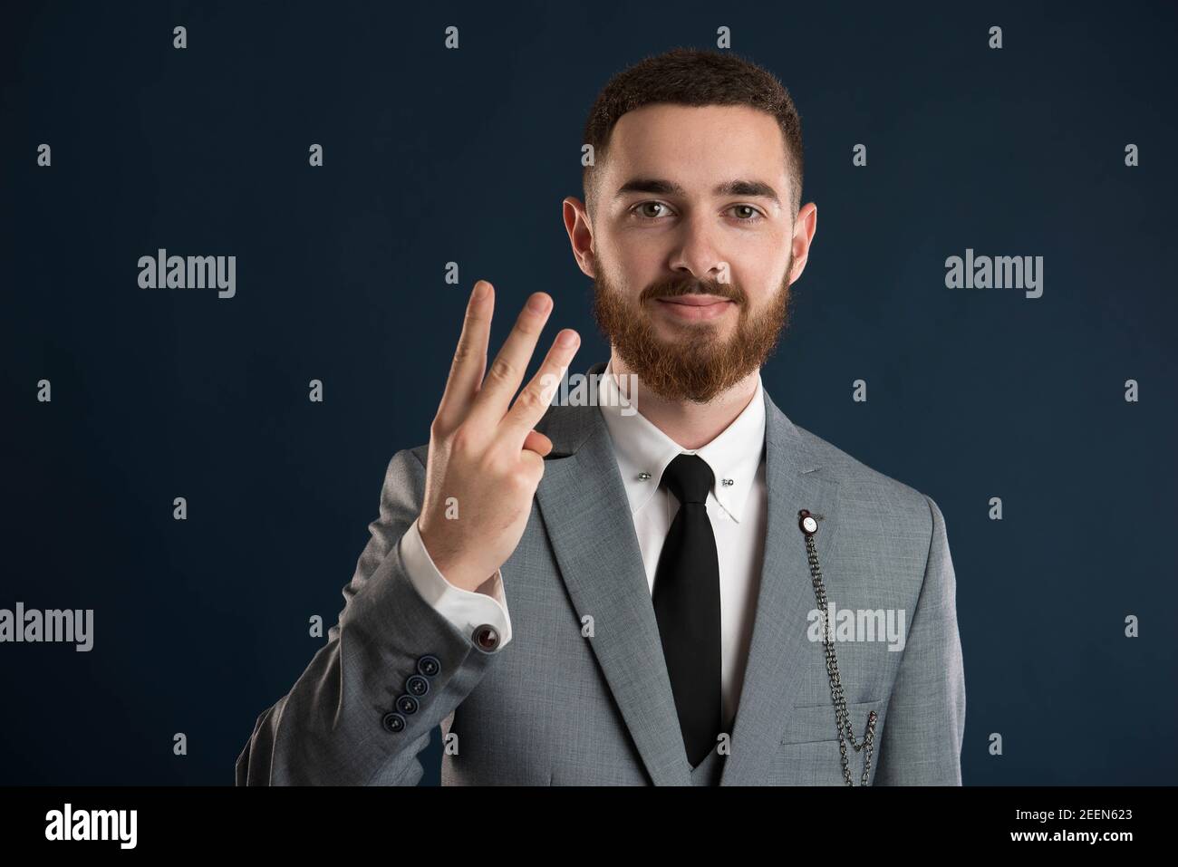 Happy businessman showing the number three wearing a grey jacket and a ...
