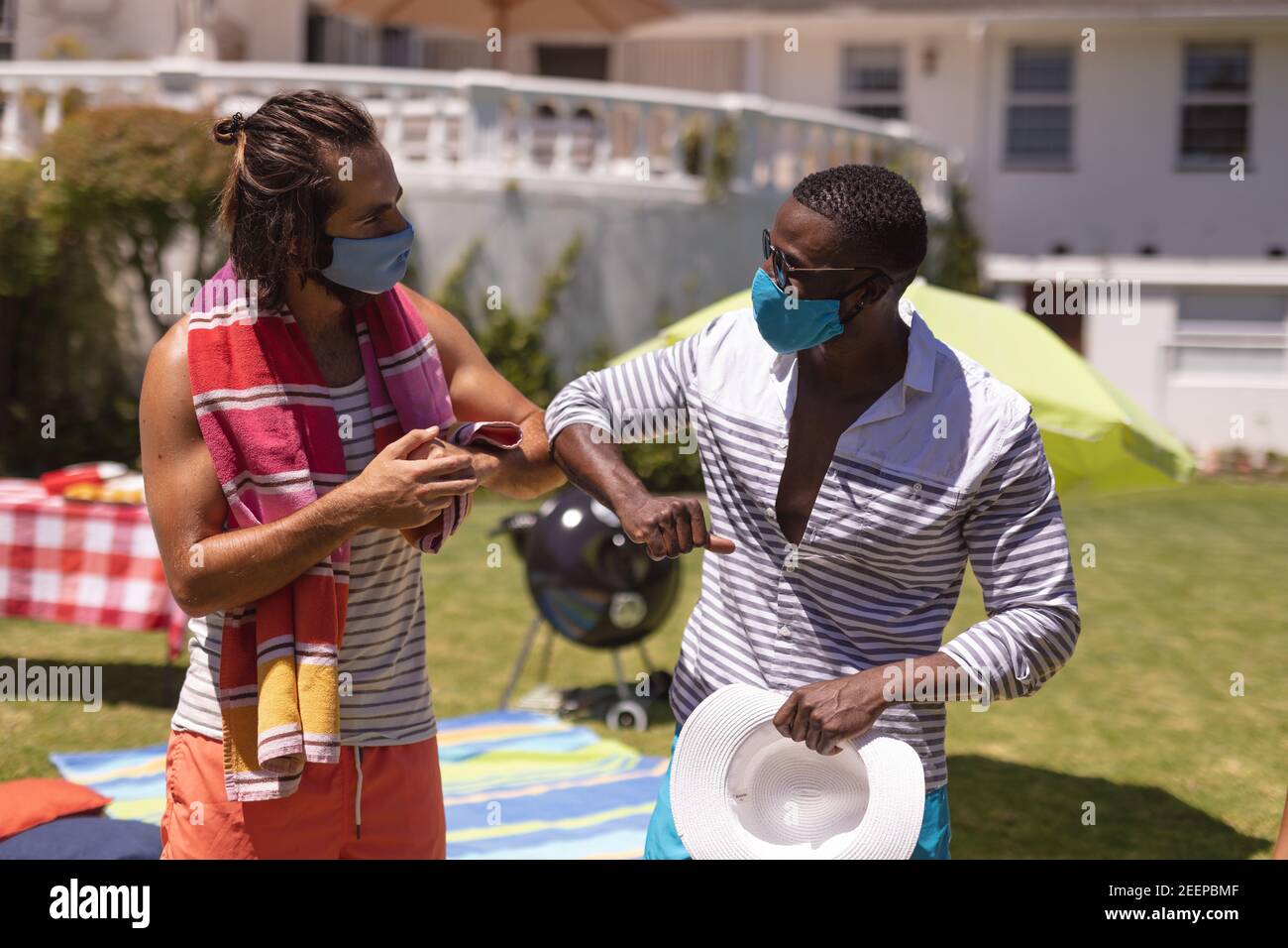 Two diverse male friends wearing face masks bumping elbows at a pool ...
