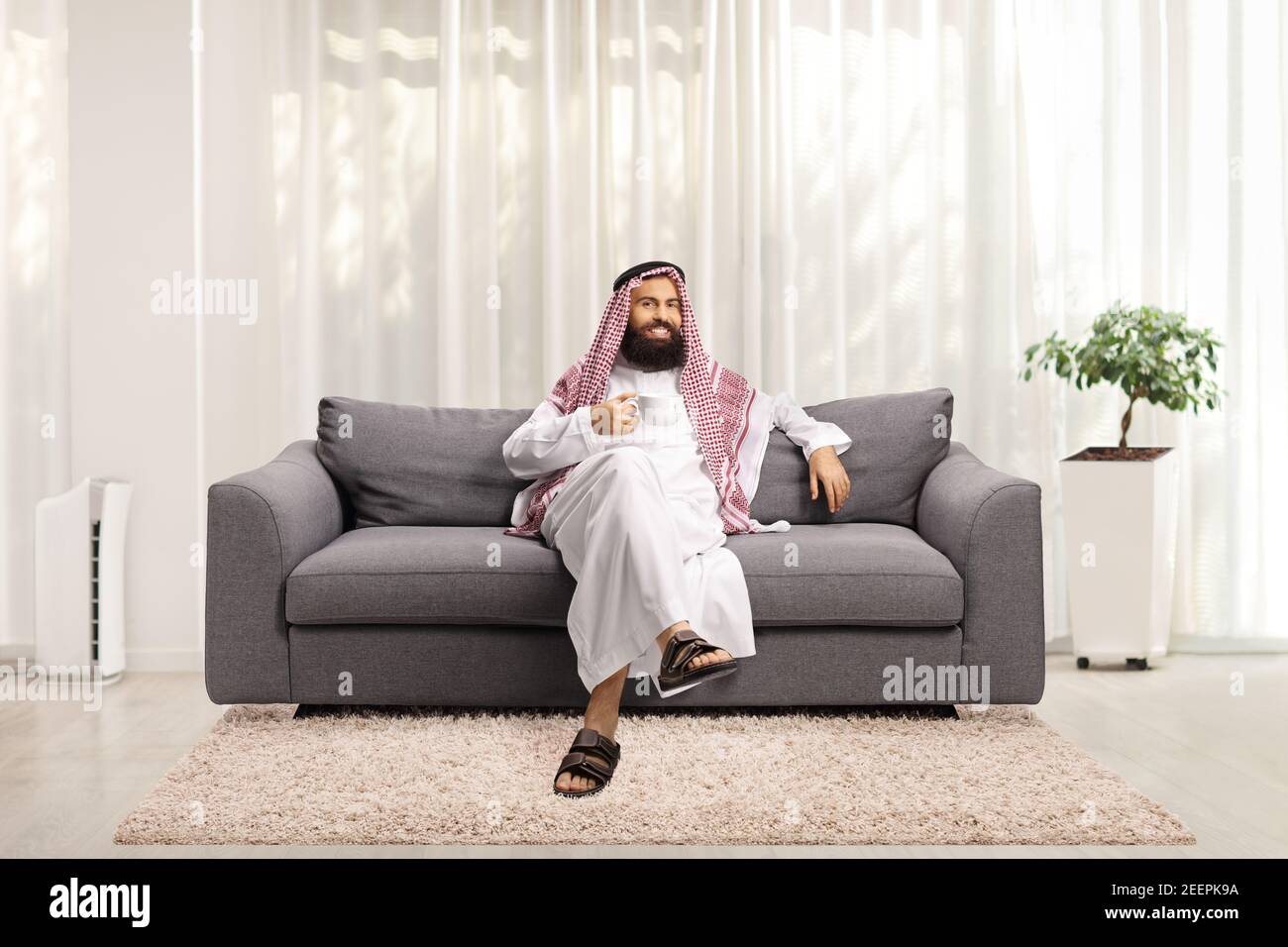 Saudi arab man sitting on a sofa at home and holding a cup of tea Stock ...