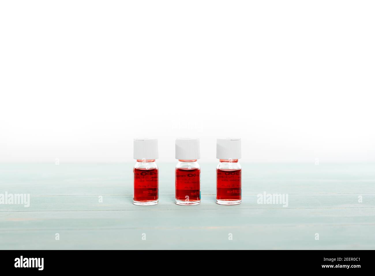 Three medicine vials filled with red liquid arranged in a row on white ...
