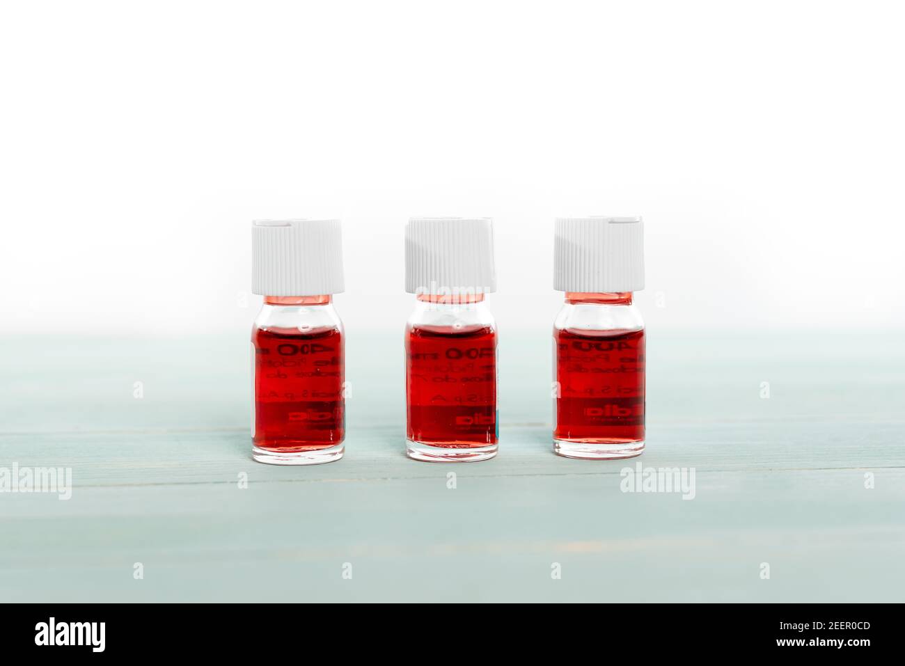 Three medicine vials filled with red liquid arranged in a row on white ...
