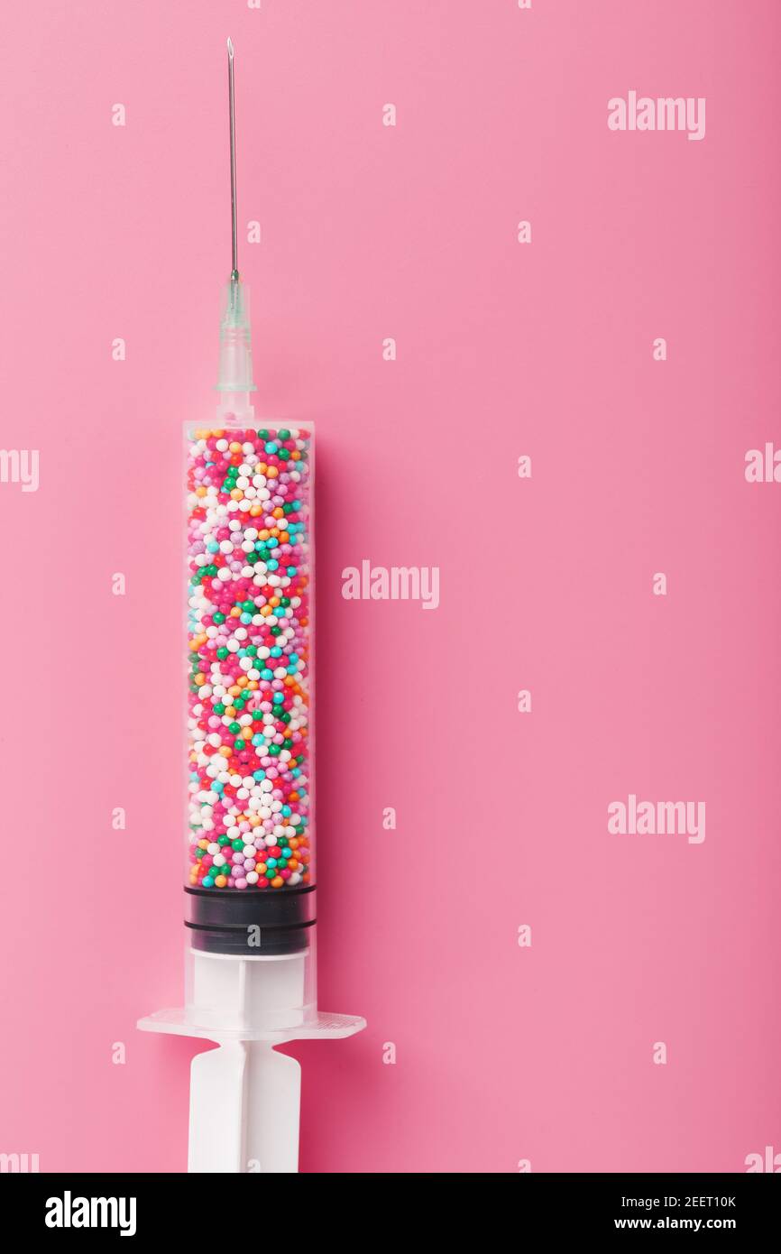 Medical Syringe filled with colorful balloons on a pink background with ...