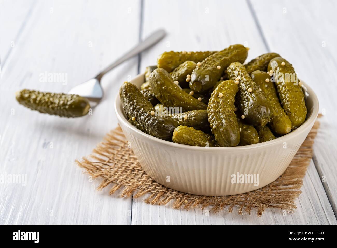 Crunchy pickled cornichons in a beige ceramic bowl and one on a fork on ...