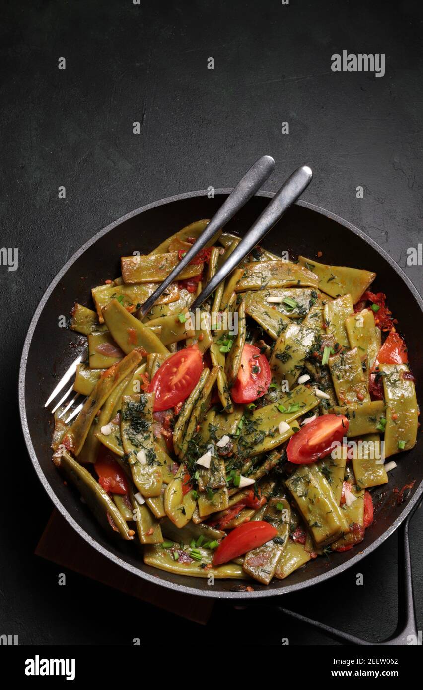 Frying pan with green beans and vegetables on dark background. Taccole ...