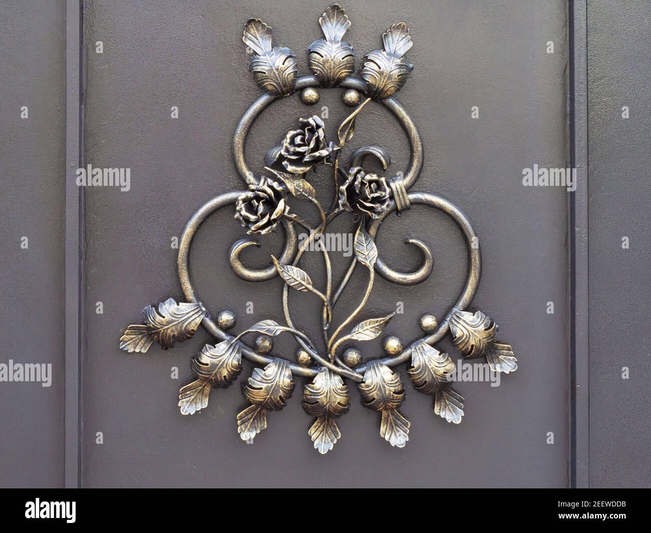 A gilded wrought iron pattern of roses, leaves and monograms on dark ...