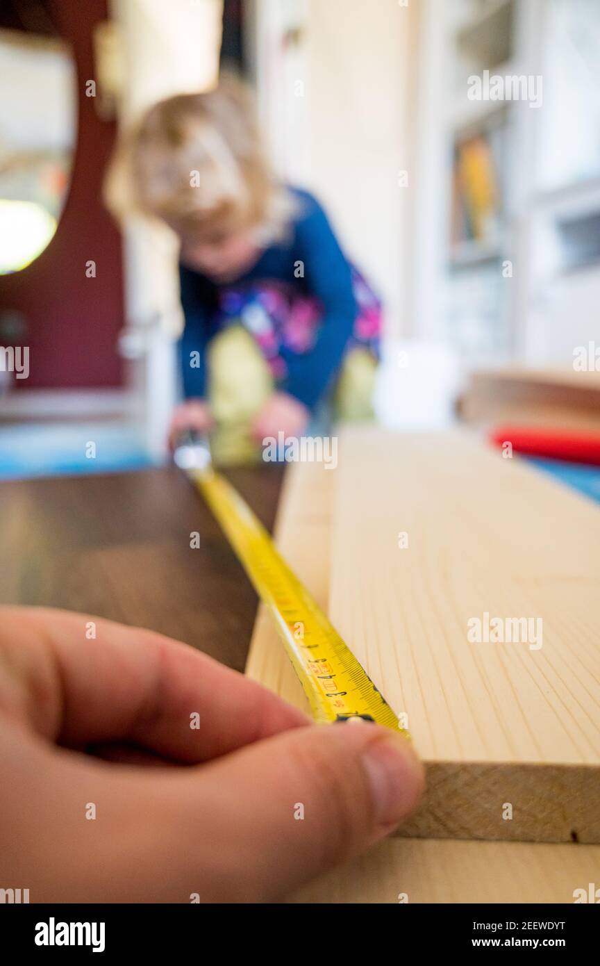 Detail of child helping with measuring wooden plank to make shelves ...
