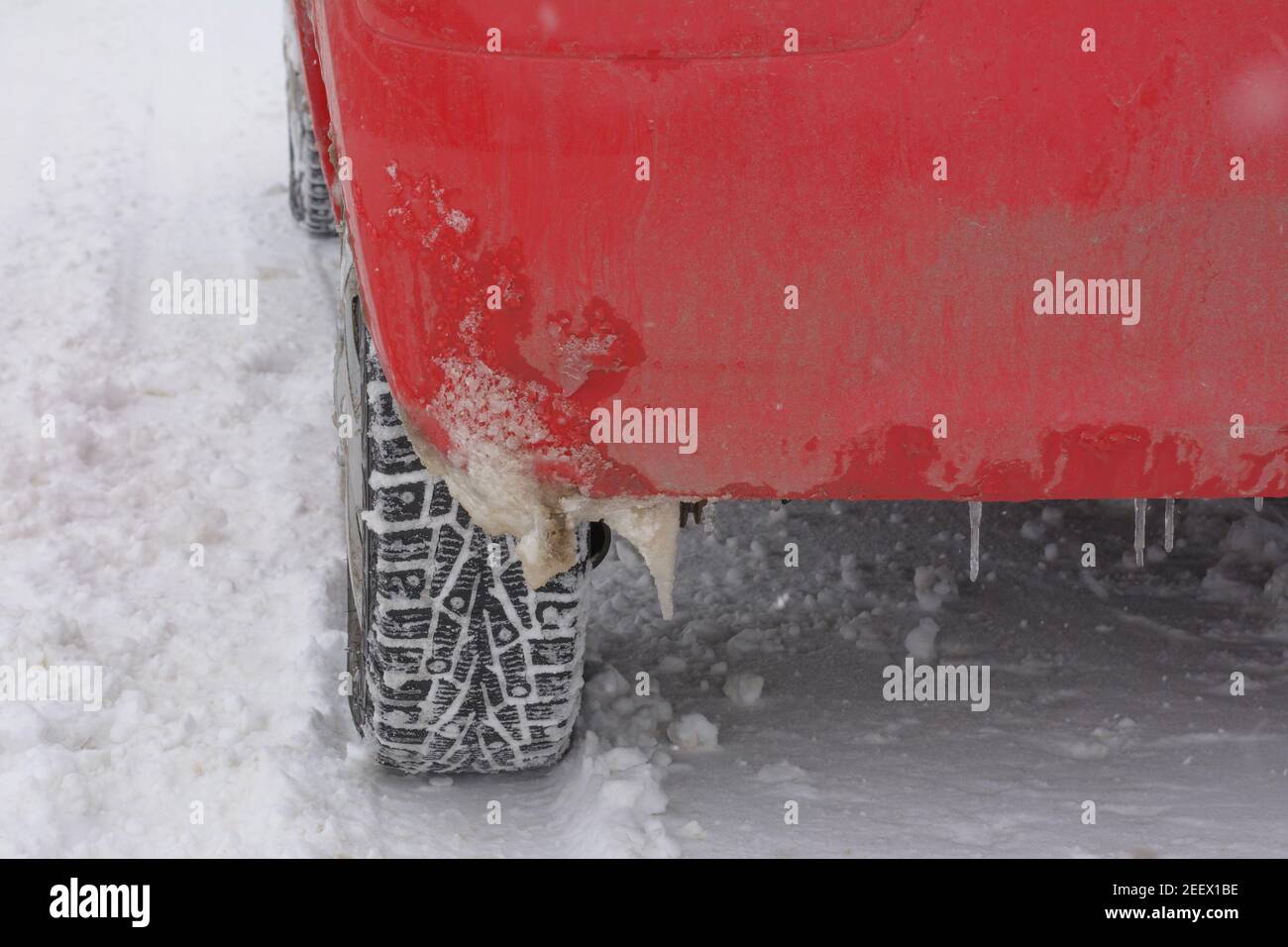 Car wheel with spikes on snowy road in winter. Icicles on bumper red ...