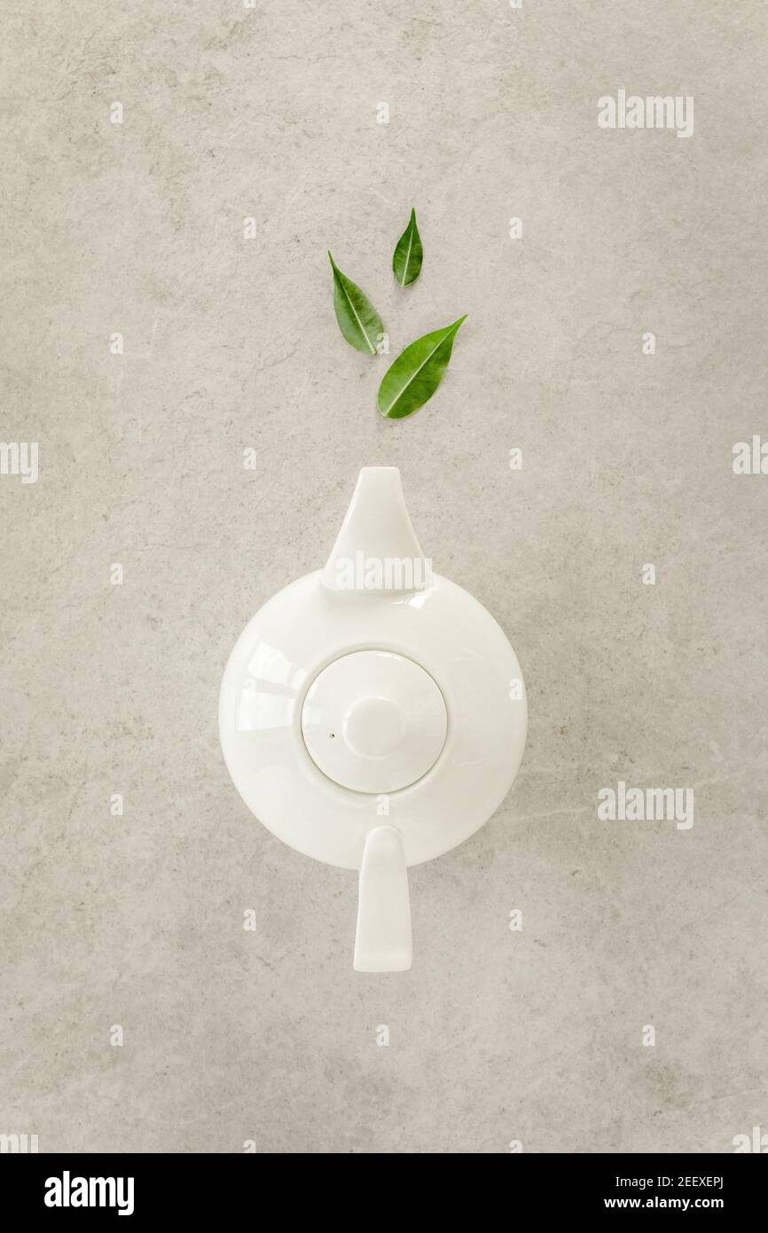 Herbal tea in a white teapot, with green tea leaves. Flat lay, top view ...