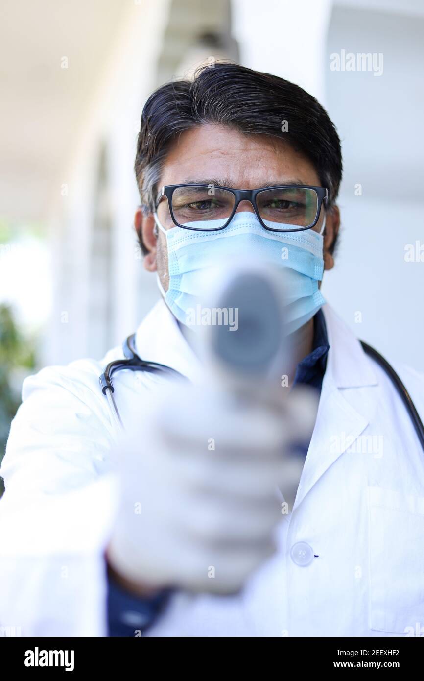 Middle-aged Indian doctor with a face mask ready to screen temperature ...