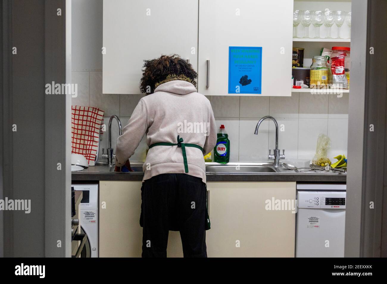 A woman washing up pots and dishes in a kitchen. Fairy Liquid visible ...