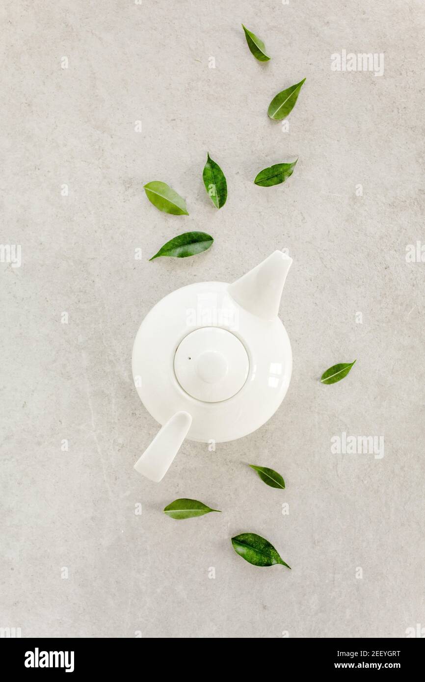 Herbal tea in a white teapot, with green tea leaves. Flat lay, top view ...