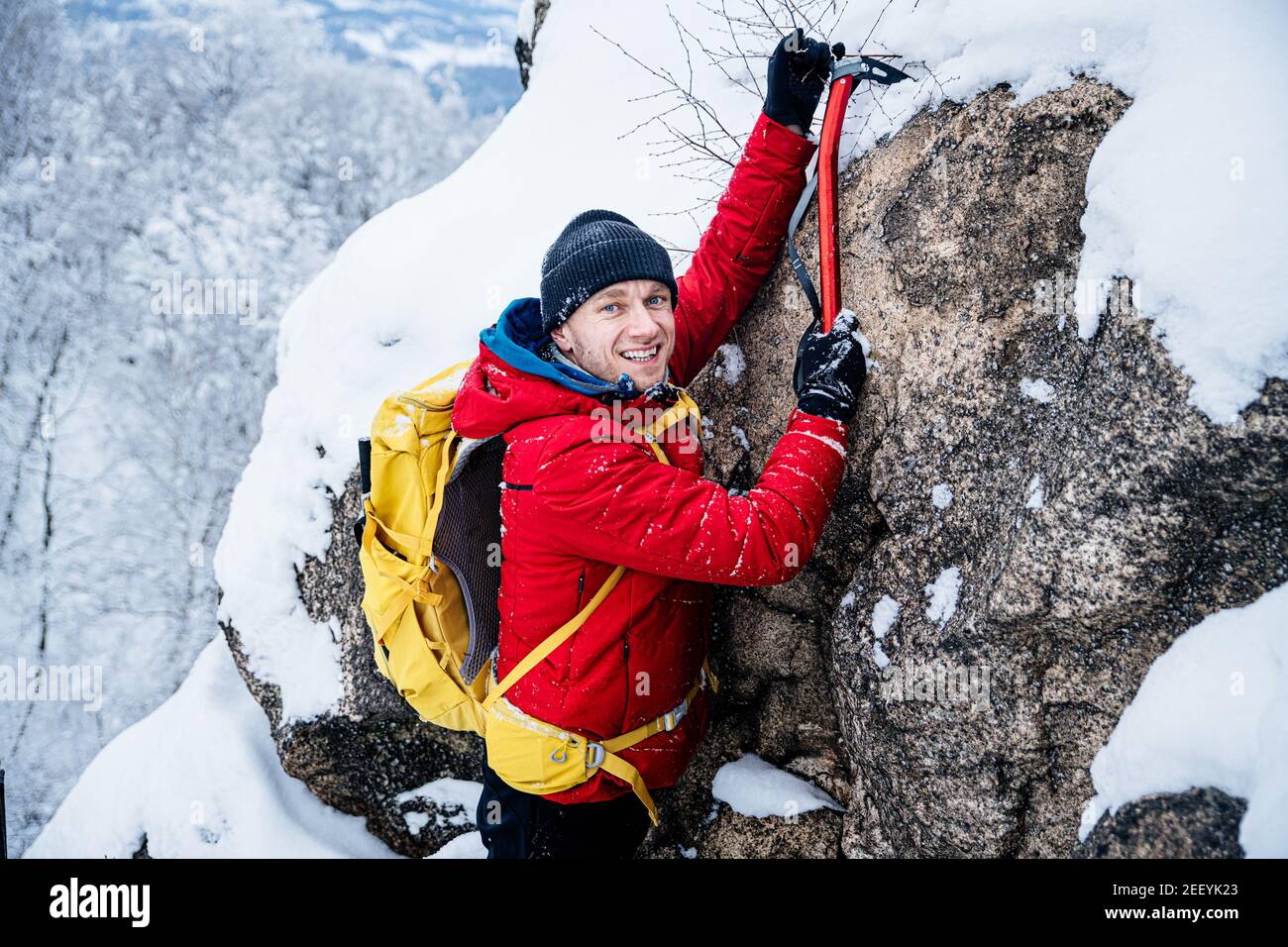 Handsome smiling mountaineer with an ice ax while climbing the rocks ...