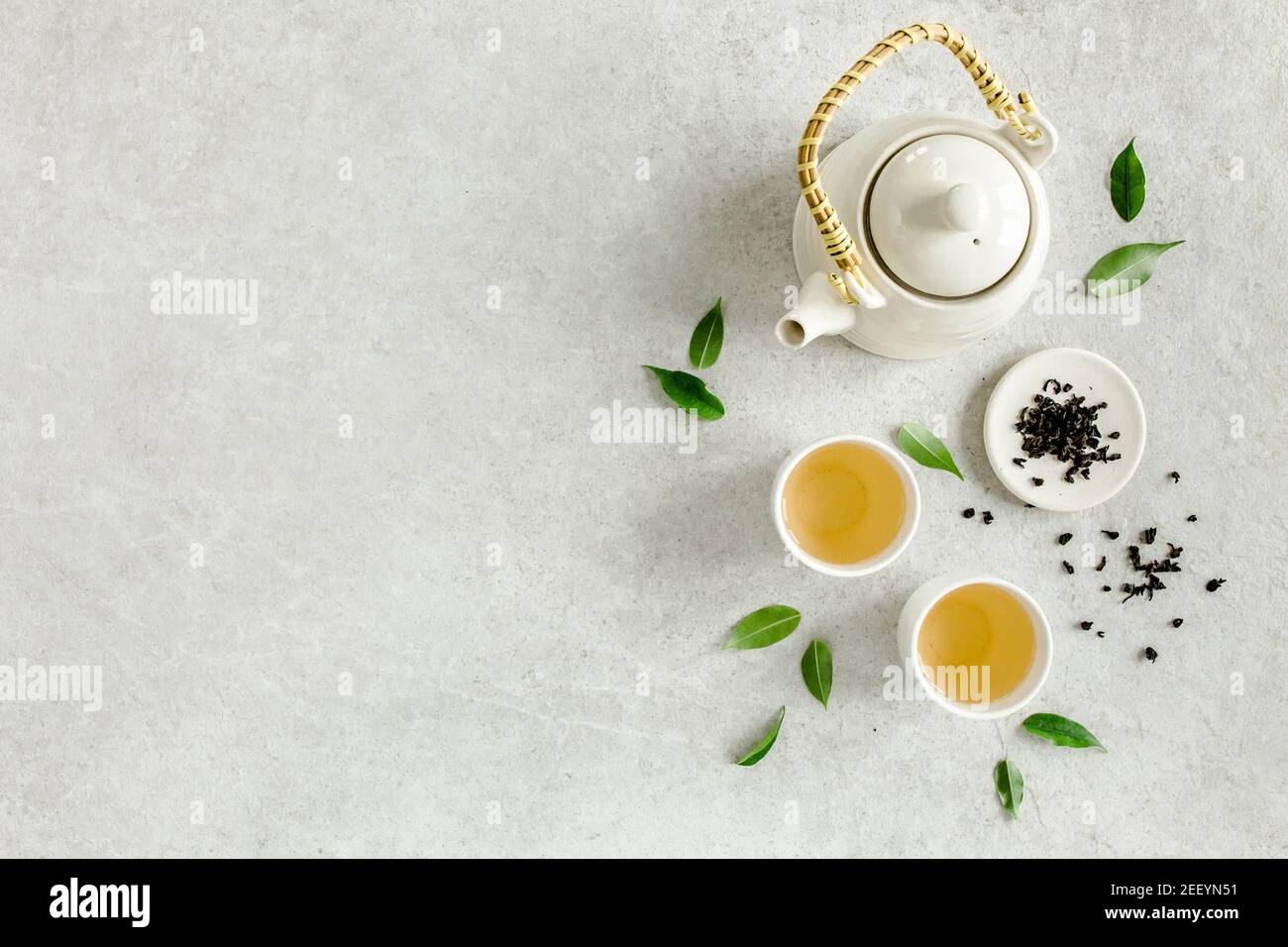 Herbal tea with two white tea cups and teapot, with green tea leaves ...