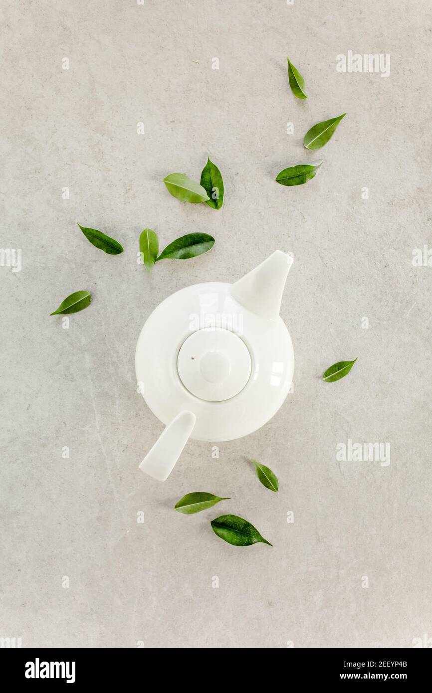 Herbal tea in a white teapot, with green tea leaves. Flat lay, top view ...