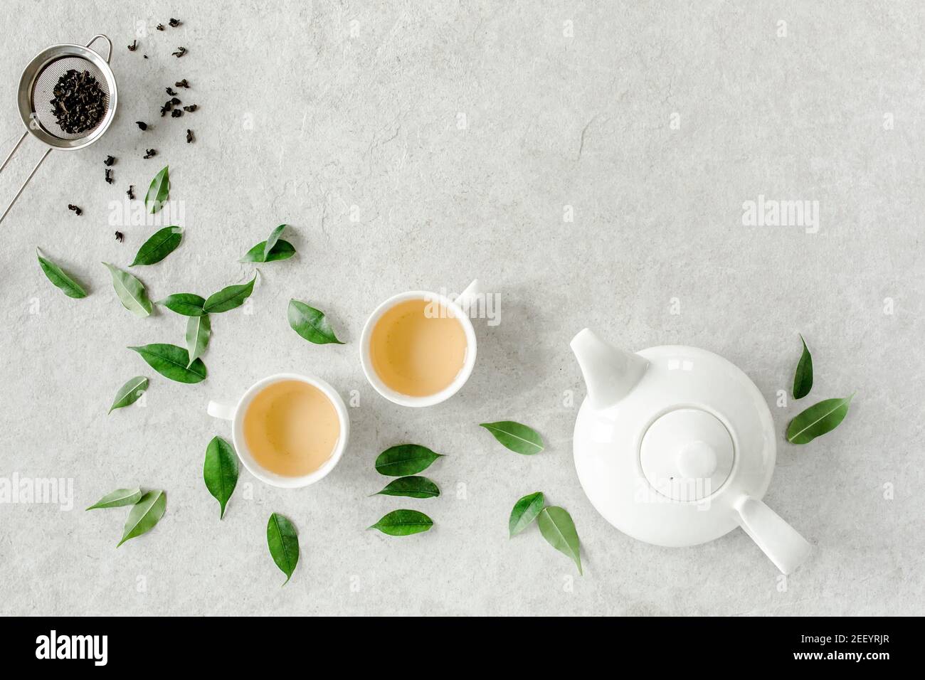 Herbal tea with two white tea cups and teapot, with green tea leaves ...