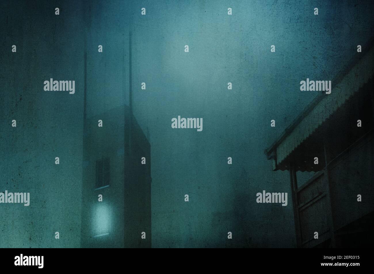 A dark moody concept of a tower with a light in the window on a foggy ...