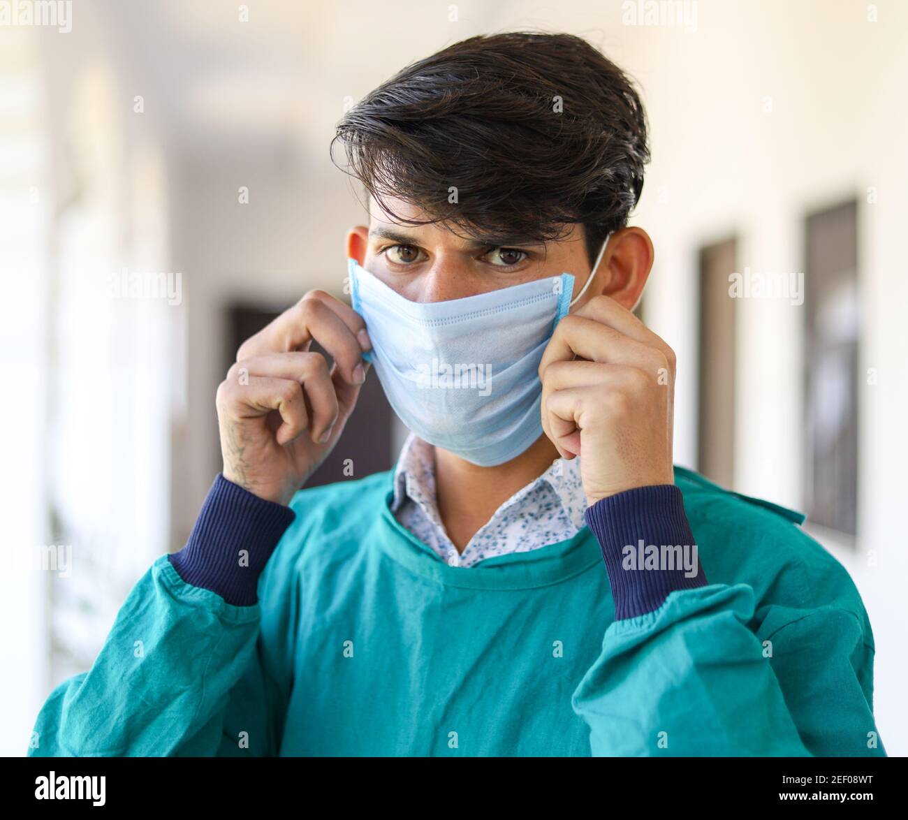 Young Indian male in surgical clothing putting on a face mask with a ...